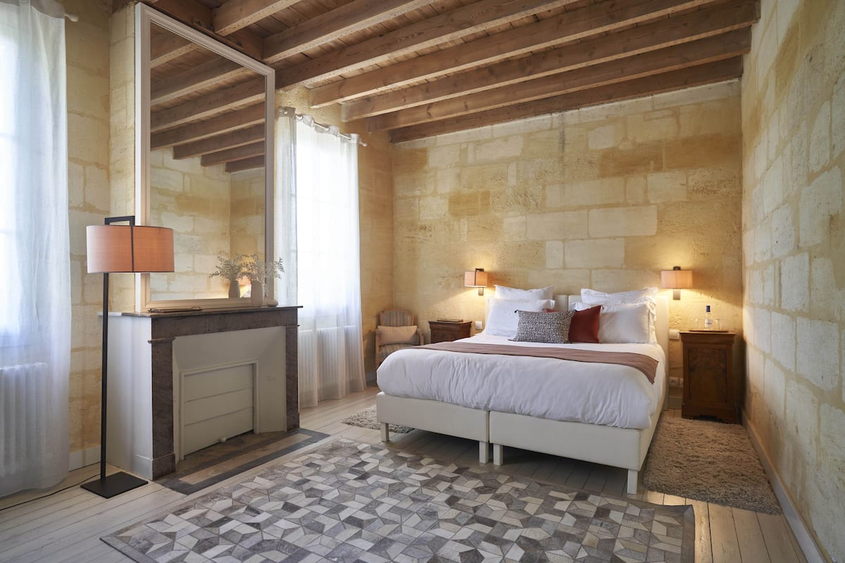 Quarto com cama, mesas de cabeceira, espelho, lareira e tapete estampado.