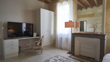 Quarto com cama, escrivaninha com televisão de tela plana, poltrona, lareira e janela com cortinas.