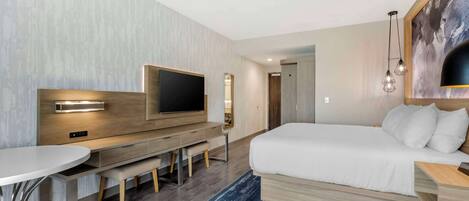 Quarto de hotel moderno com uma cama grande, uma escrivaninha com cadeira, uma televisão de tela plana e uma mesa de jantar.