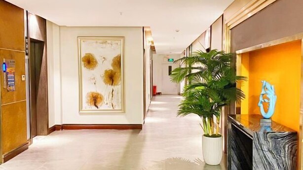 Um saguão de hotel com um balcão de recepção, uma grande pintura abstrata na parede e uma planta em vaso.