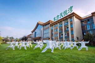 Um grupo de pessoas praticando Tai Chi em frente a um edifício com elementos arquitetônicos tradicionais e modernos.