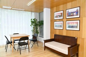 Um quarto com piso de madeira, sofá de madeira, uma mesa com cadeiras e quadros nas paredes.