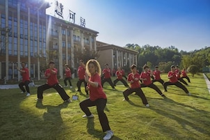 Um grupo de pessoas de camisas vermelhas praticando uma rotina de exercícios ao ar livre.