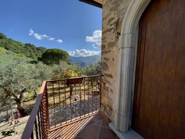 Uma varanda com vista para uma paisagem montanhosa, um muro de pedra e uma porta de madeira.