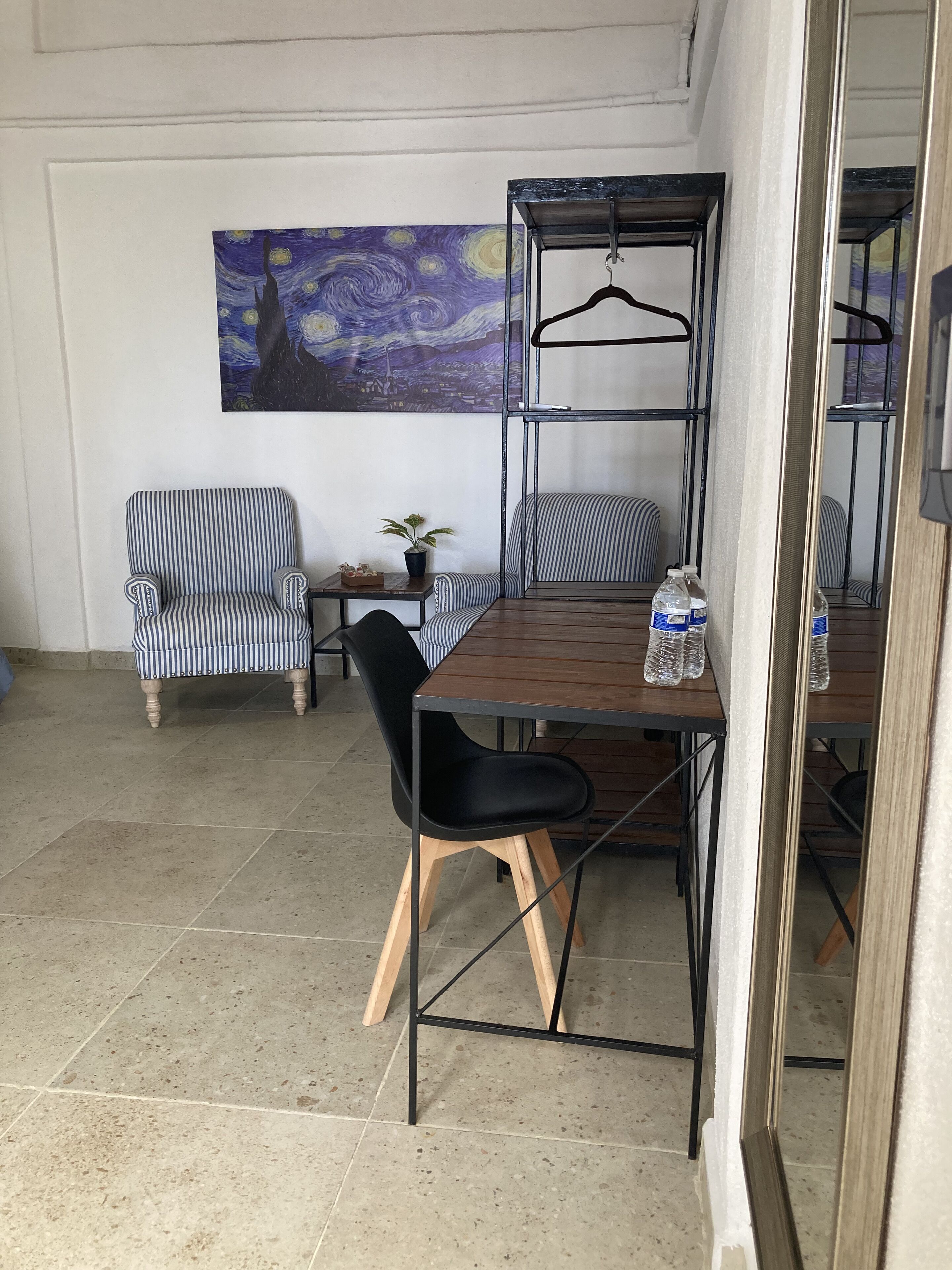 Um quarto com uma mesa de madeira, poltronas listradas, uma cadeira preta, uma pequena mesa com uma planta e um quadro de estrelas na parede.