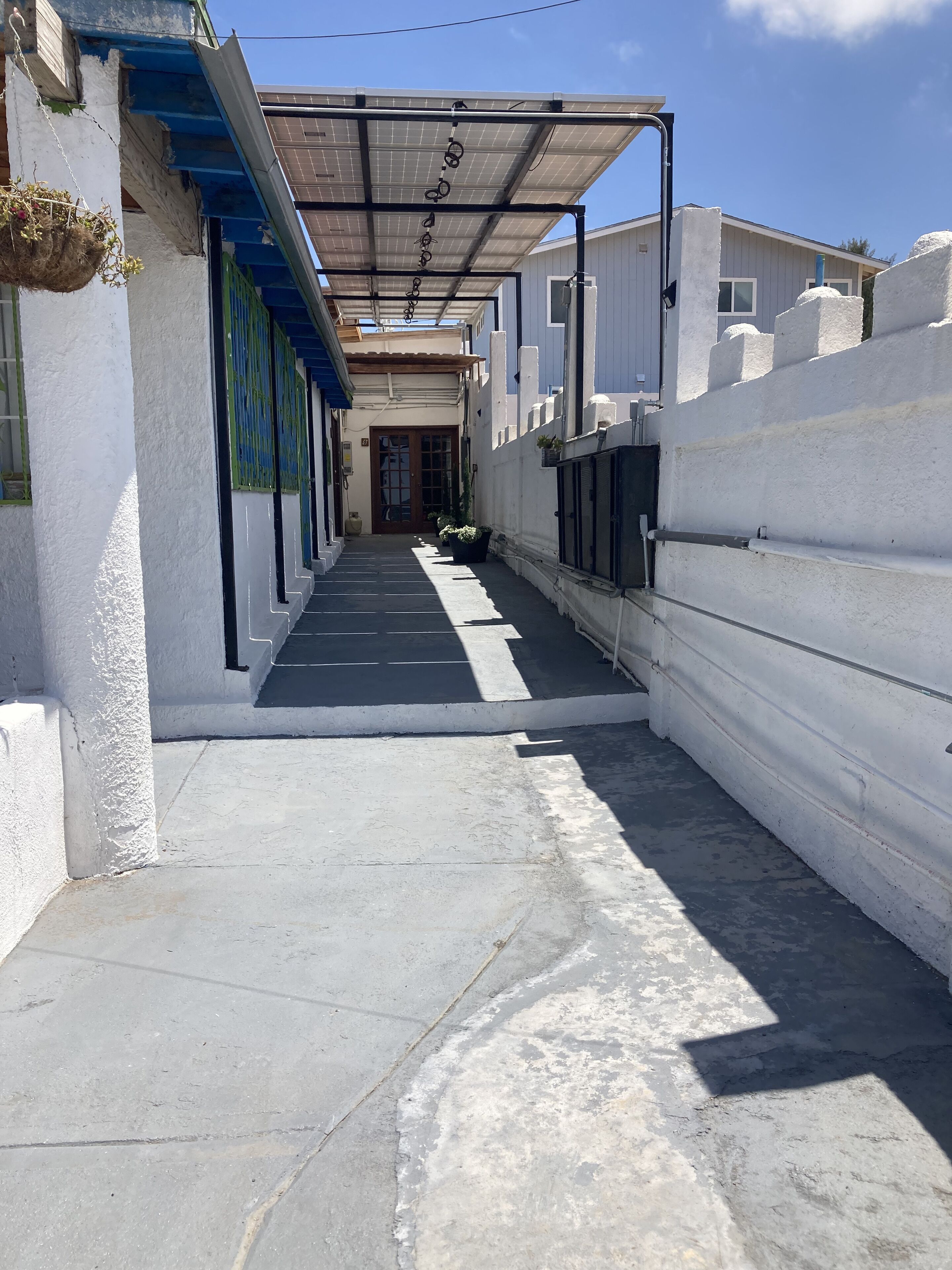 Um beco estreito com galeria coberta, paredes brancas e uma porta azul.