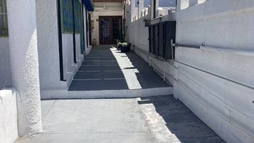 Um beco estreito com galeria coberta, paredes brancas e uma porta azul.