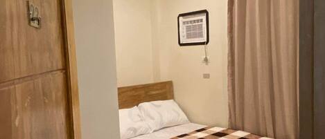 Quarto com cama de madeira, luminária no teto, ar-condicionado fixado na parede e porta com fechadura.