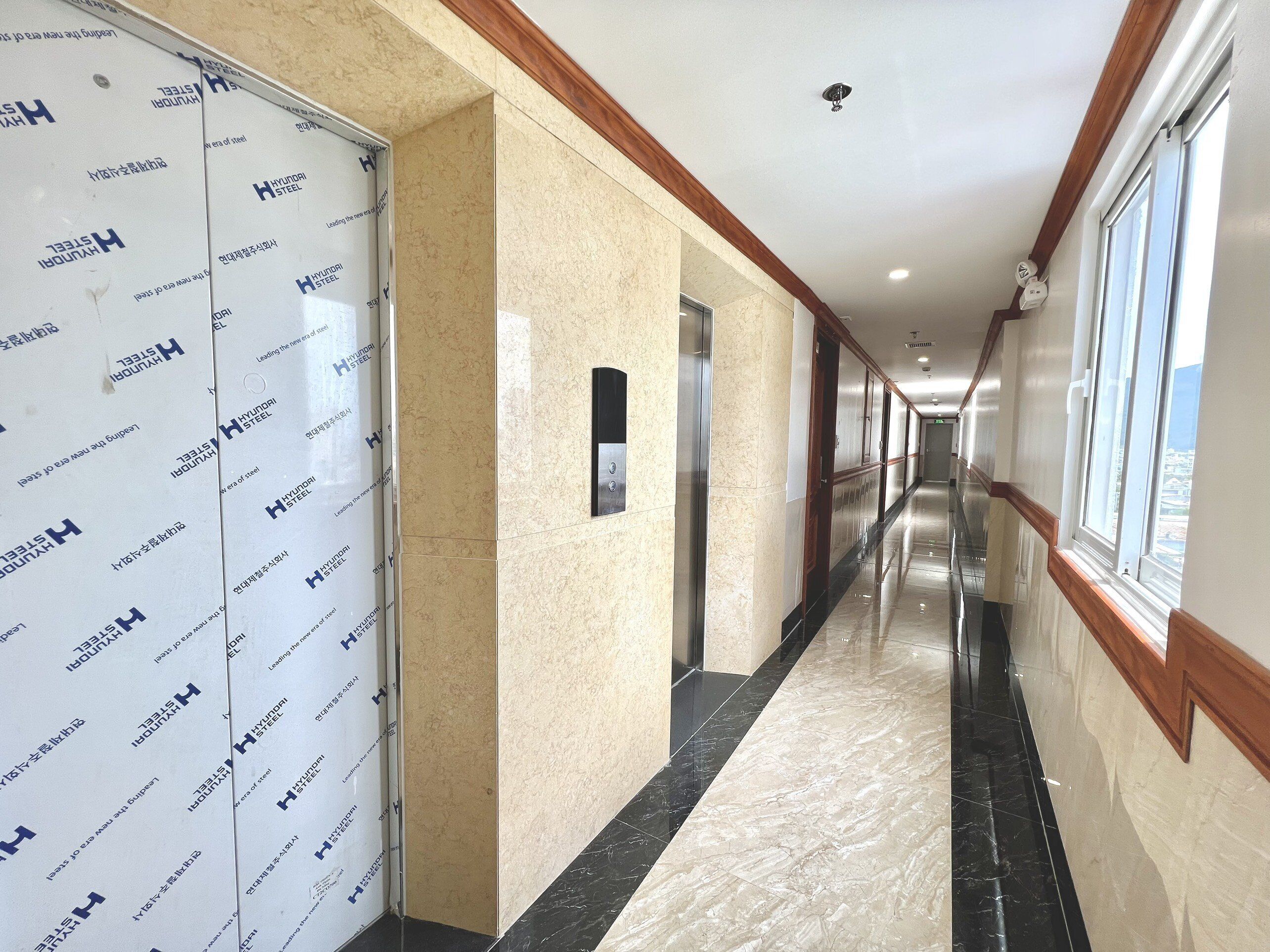 Corredor de hotel com piso de mármore, detalhes em madeira e janelas amplas.