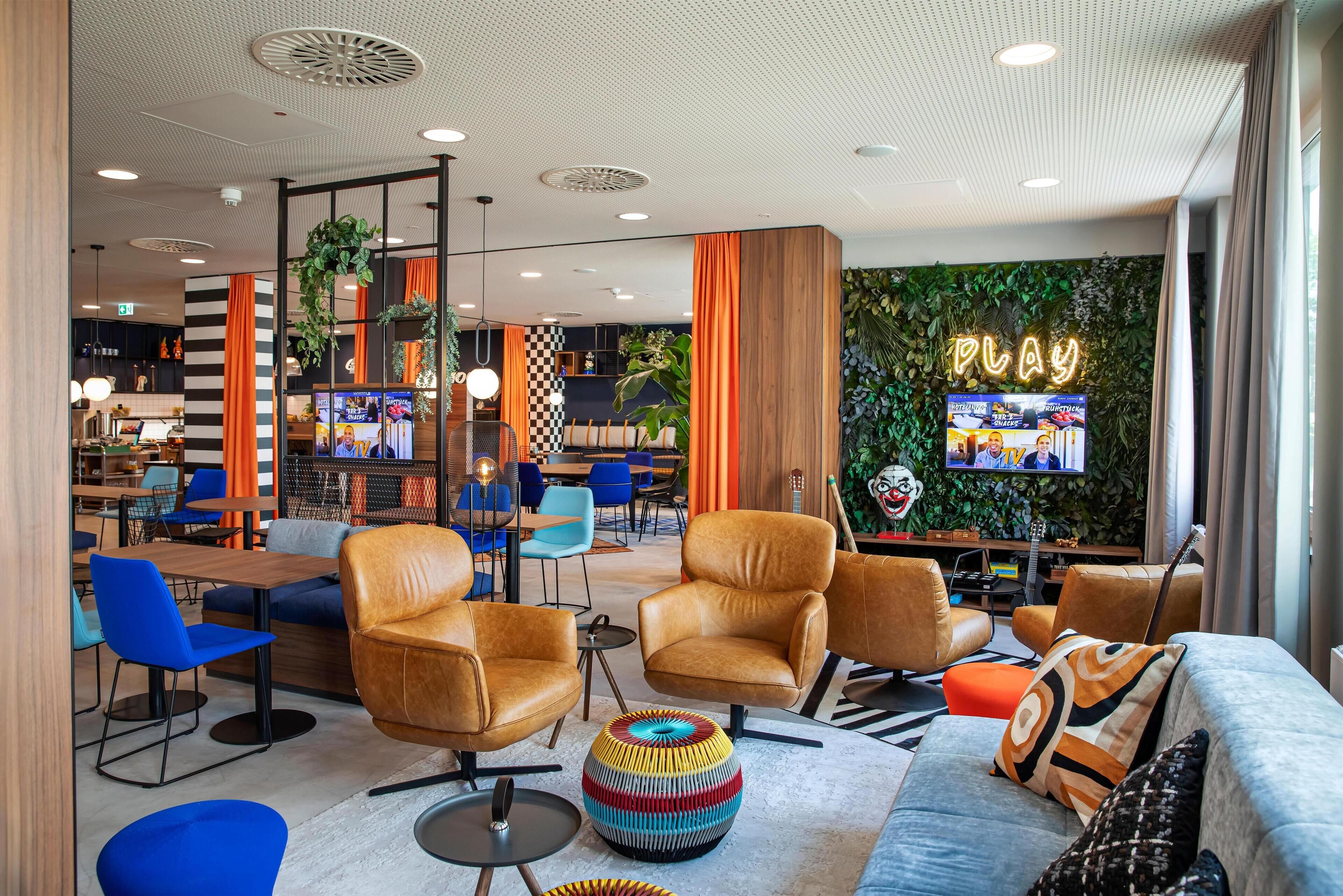 Uma área de estar moderna com poltronas de couro, um banquinho colorido e um letreiro neon com a palavra 'PLAY'.