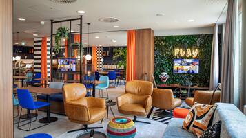 Uma área de estar moderna com poltronas de couro, um banquinho colorido e um letreiro neon com a palavra 'PLAY'.