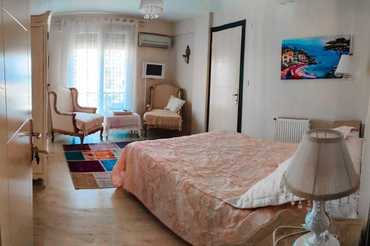 Quarto com cama, cadeira, escrivaninha, luminária e um quadro na parede.