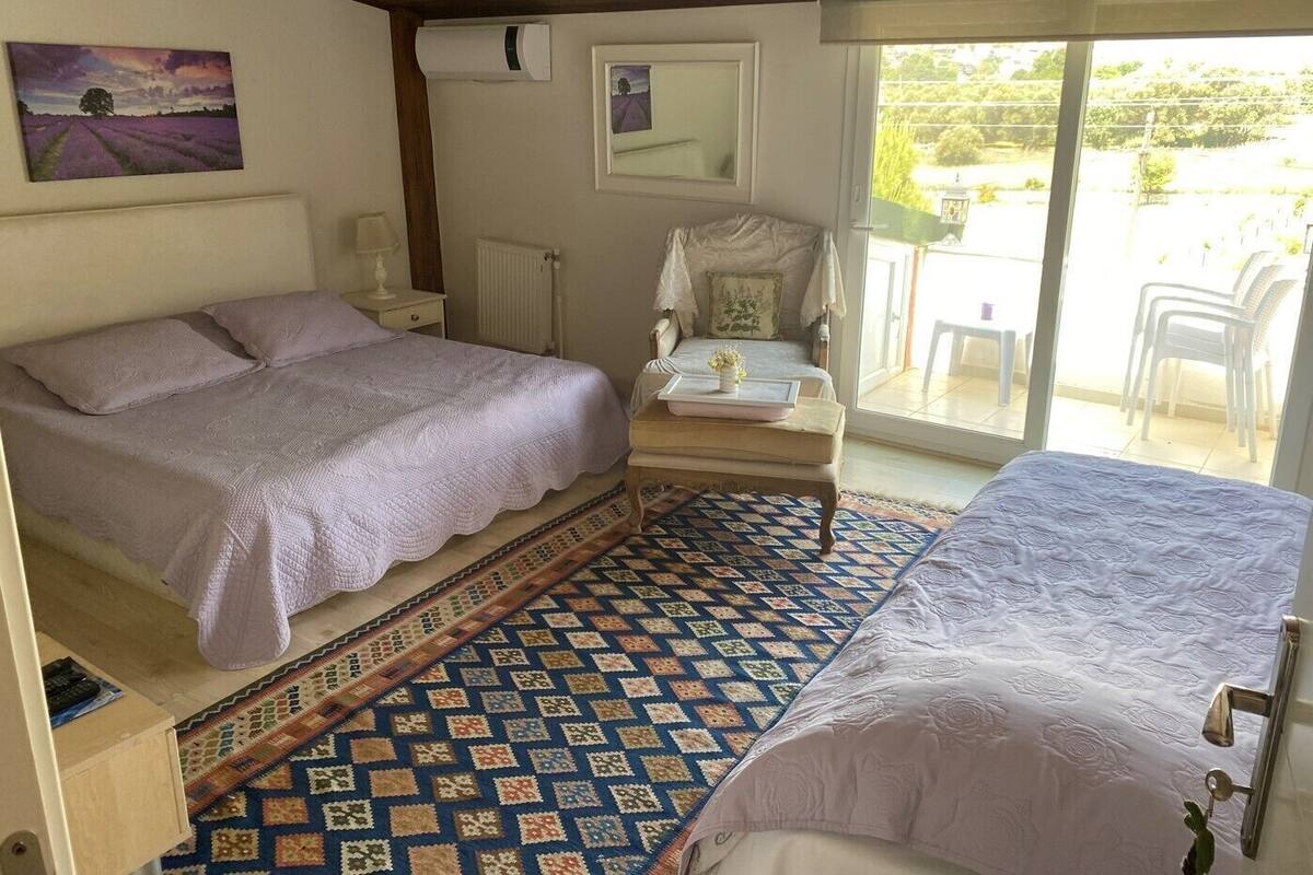 Quarto com duas camas, um tapete estampado, uma cadeira e vista para o exterior.