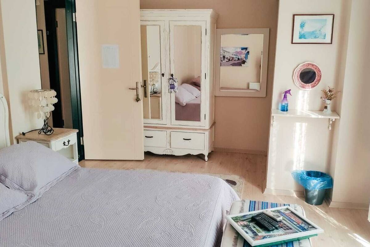Quarto com cama, guarda-roupa, mesa de cabeceira, espelho e janela com cortinas.