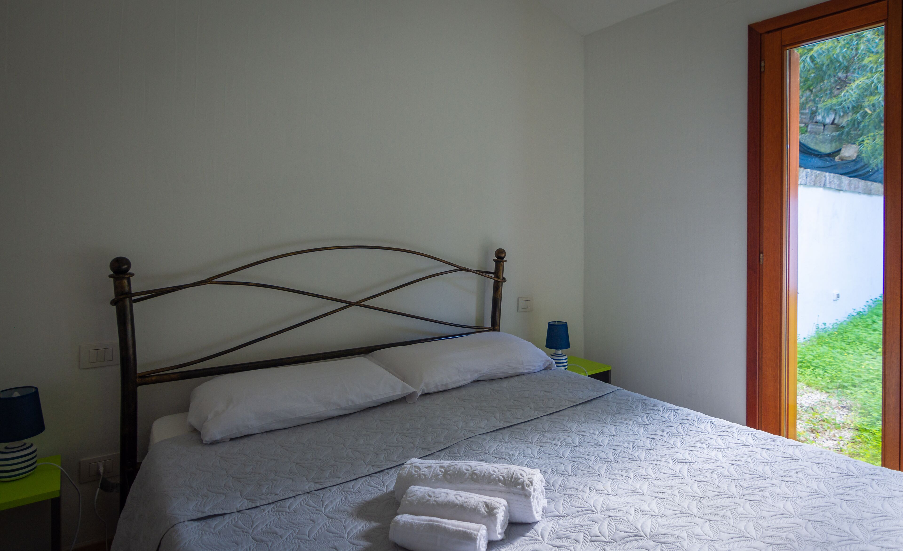Cama com cabeceira, almofadas e manta. Duas mesas de cabeceira com abajures.