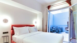 Quarto de hotel com uma cama grande, uma mesinha de apoio e vista para uma área de estar externa através de uma porta de vidro deslizante.