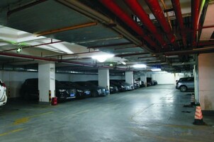 Garagem subterrânea de estacionamento com várias fileiras de carros estacionados e elementos estruturais visíveis, como pilares e tubulações.