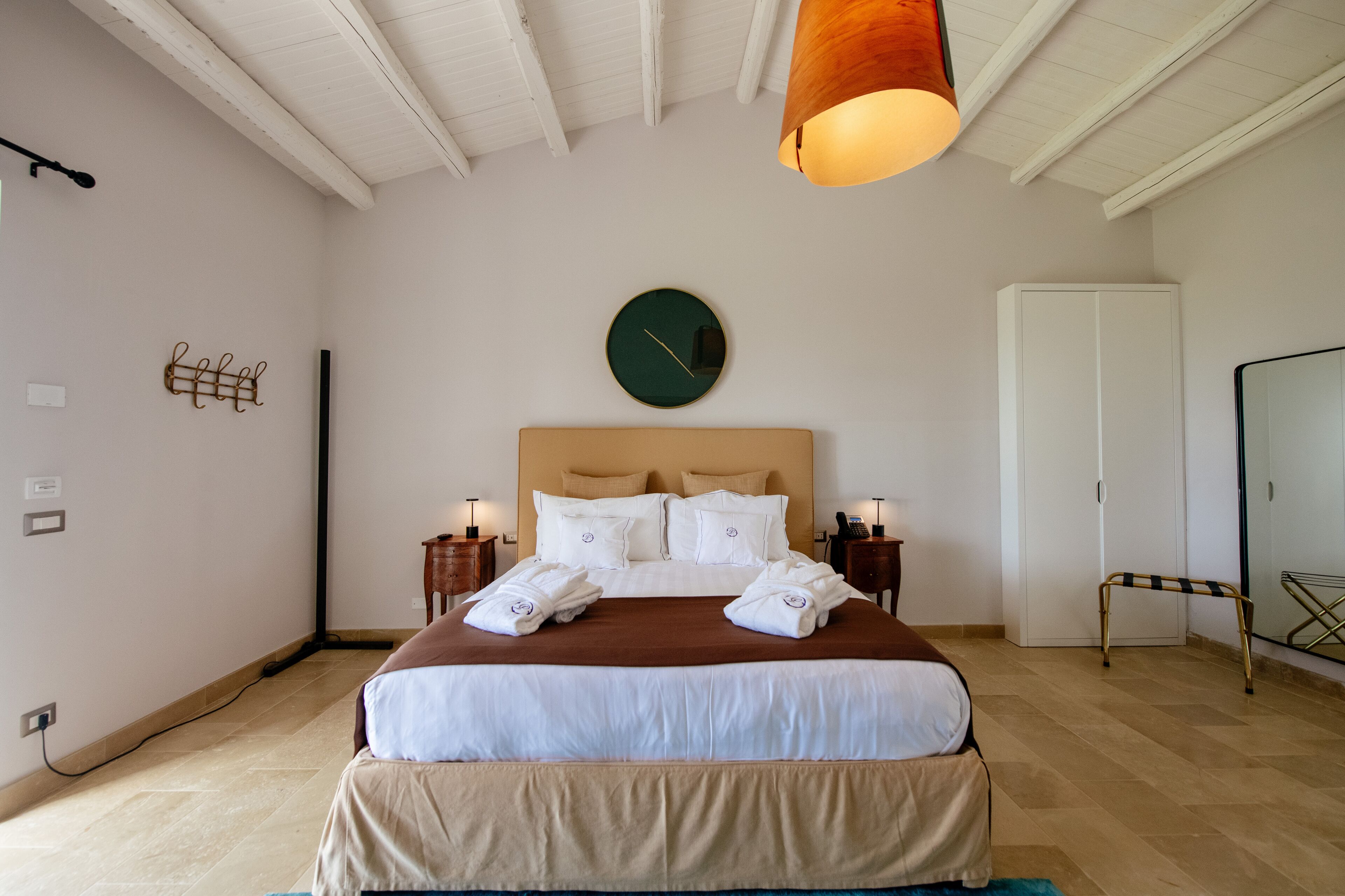 Quarto de hotel com cama grande, cabeceira de madeira, relógio de parede redondo, abajures e guarda-roupa.