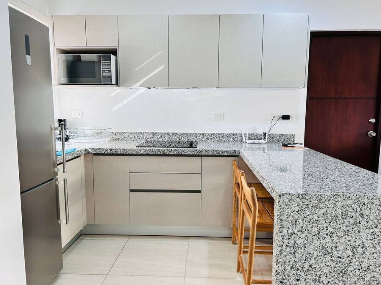 Cozinha com bancada de granito, eletrodomésticos de aço inoxidável e cadeiras de madeira.