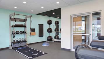 Ginásio com equipamentos de exercício, um espelho grande e uma porta que dá para o exterior.