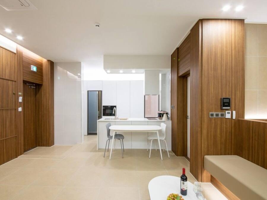 Quarto de hotel moderno com parede revestida de madeira, área de refeições branca e pequena cozinha compacta.