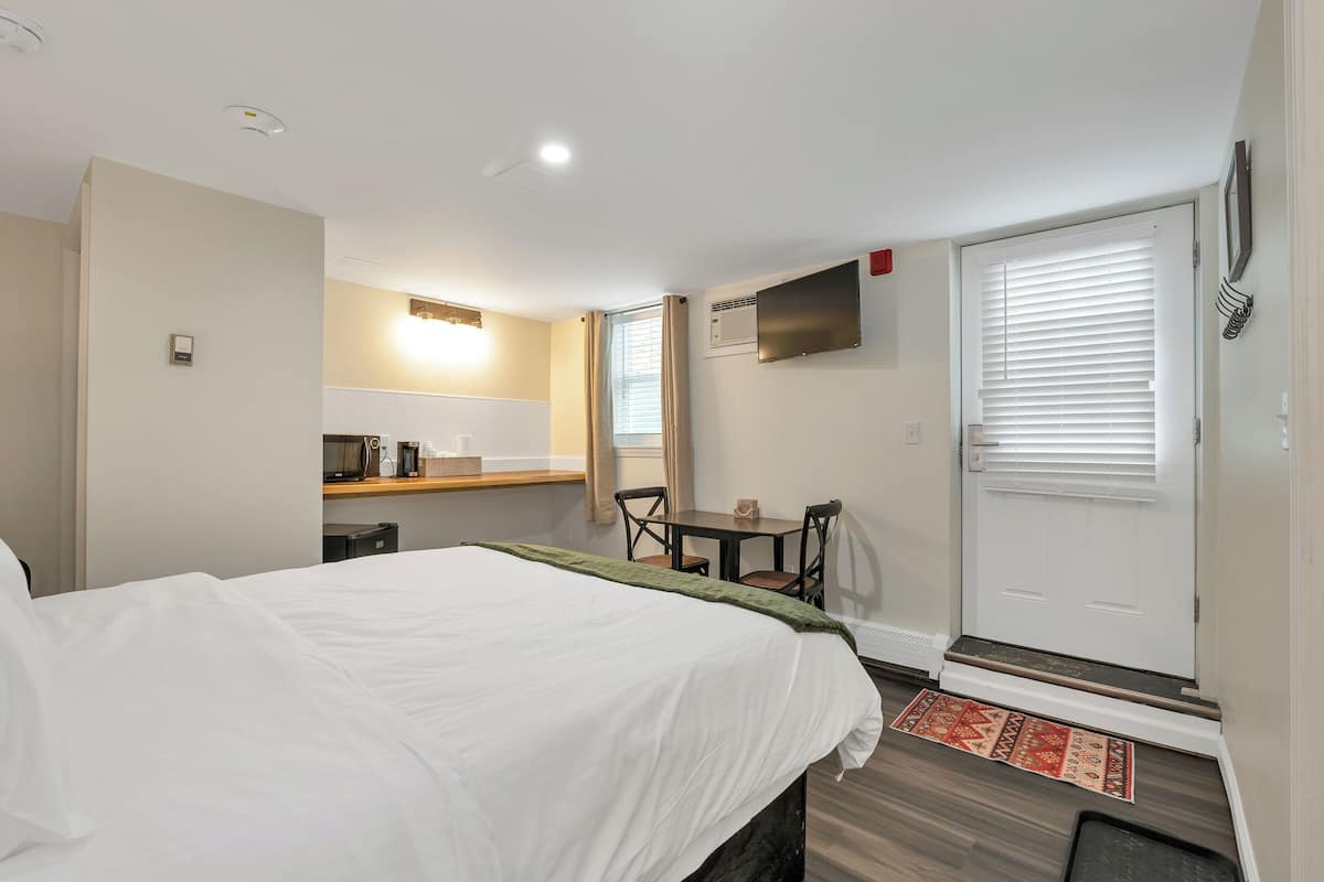 Quarto de hotel com cama, uma pequena mesa com cadeiras, cozinha compacta, televisão na parede e porta de correr.