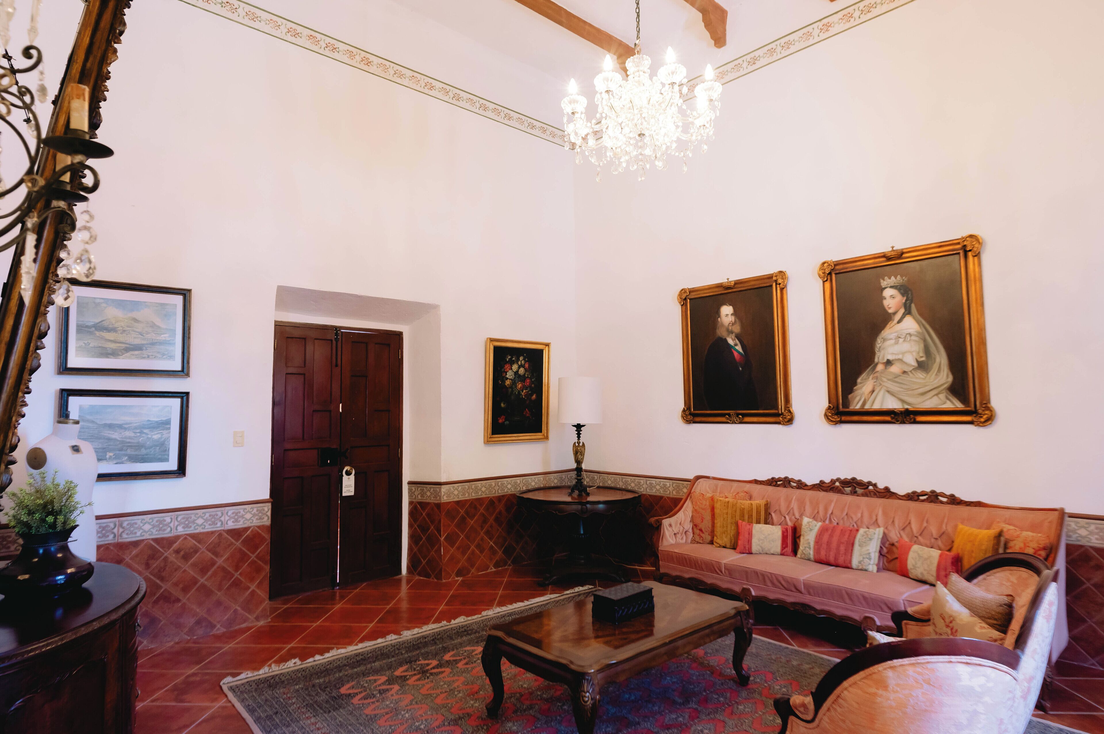Um quarto com um candelabro, um sofá, uma mesa de centro e dois retratos emoldurados na parede.