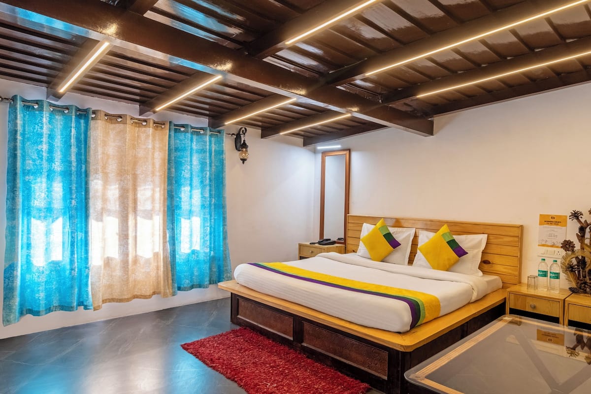 Um quarto com uma cama de madeira, um tapete vermelho e uma mesa de cabeceira com abajur.