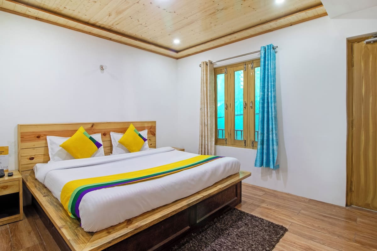 Um quarto bem organizado com uma cama de madeira, uma mesa de cabeceira, uma janela com cortinas e uma porta de madeira.