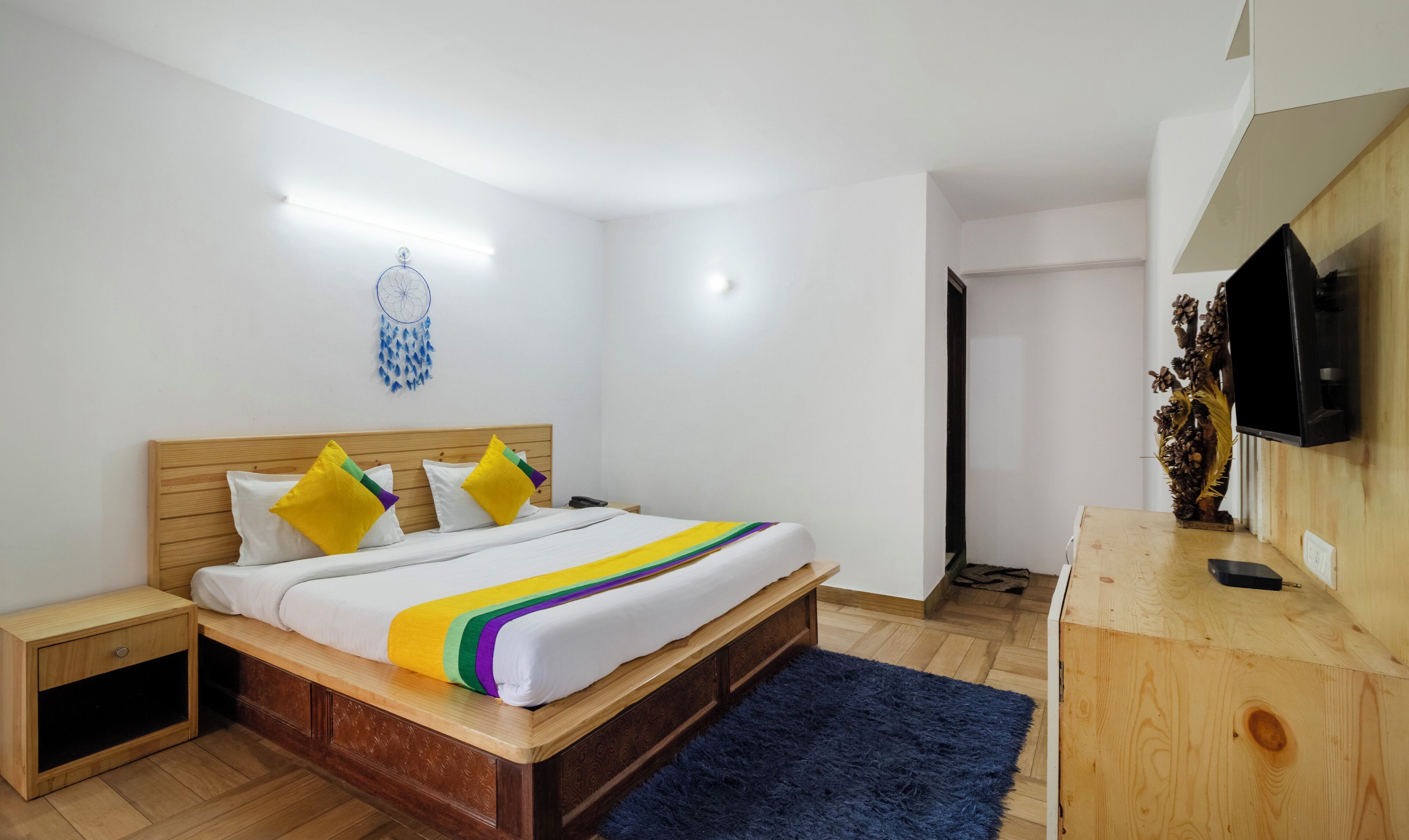 Quarto moderno com cama de madeira, roupa de cama branca e almofadas coloridas.
