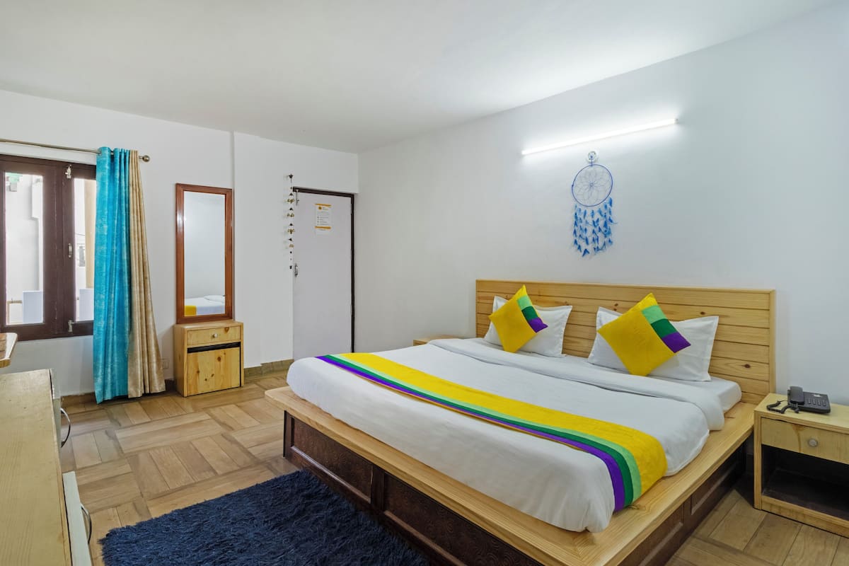Quarto com cama de madeira, mesa de cabeceira com telefone, espelho e um adorno de pena na parede.