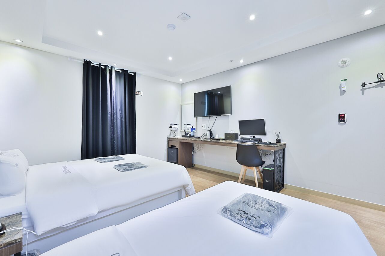 Quarto de hotel com duas camas, uma mesa com computador, televisão e banheiro.