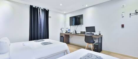 Quarto de hotel com duas camas, uma mesa com computador, televisão e banheiro.