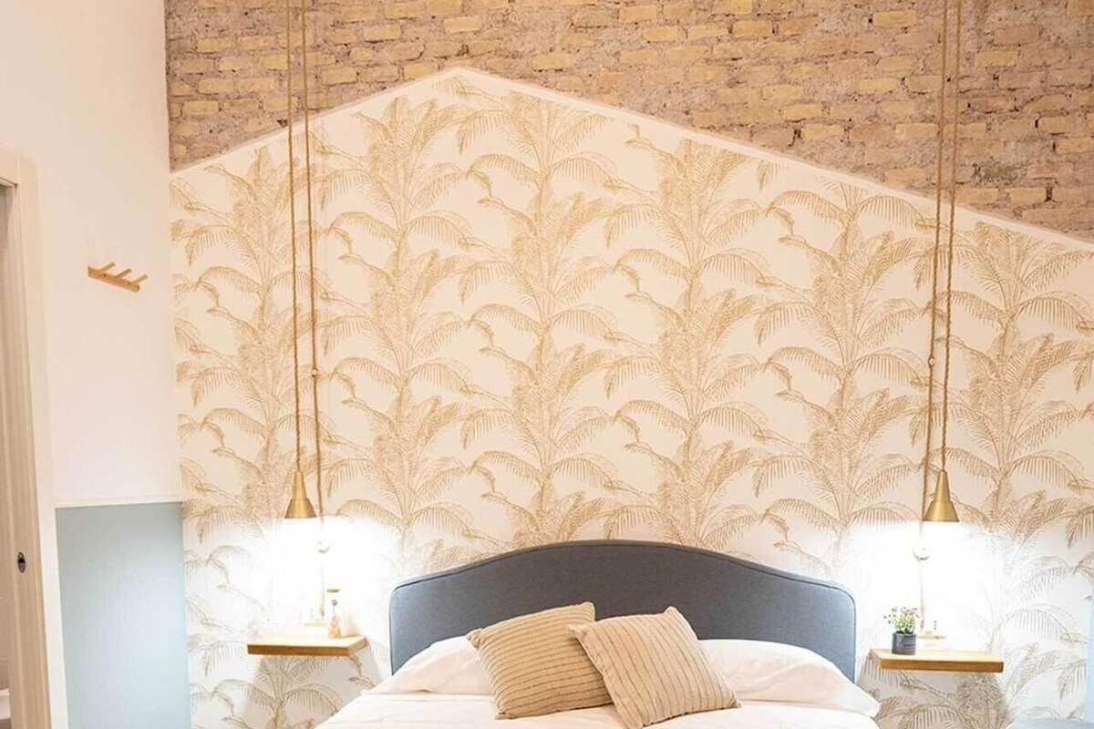 Quarto com uma cama grande, parede de destaque em tijolo e duas mesas de cabeceira com luminárias.