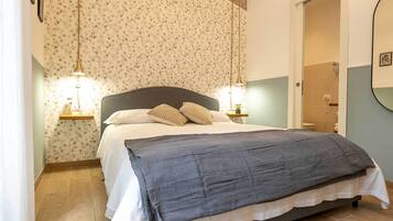 Cama bem arrumada com manta cinza, duas luminárias laterais e papel de parede estampado com motivos florais.
