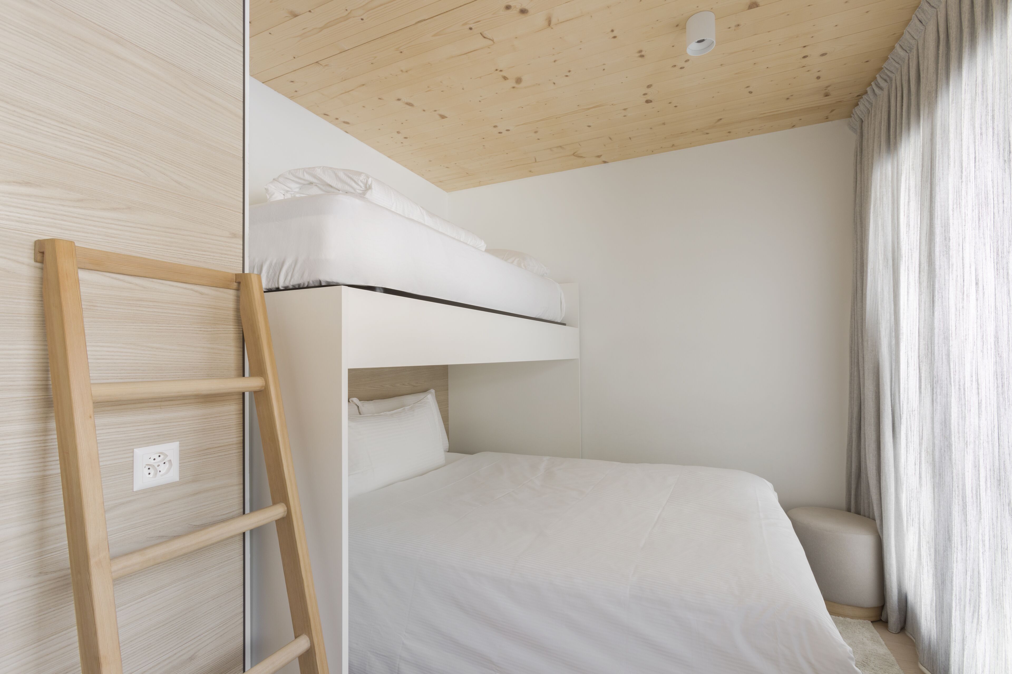 Uma cama beliche com escada de madeira, colchão branco e parede em tom claro.