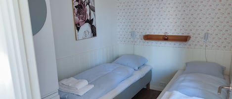 Acomodação pequena, com um quarto e duas camas, uma prateleira de madeira e parede com padrão floral.