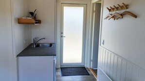 Um corredor estreito com uma área de cozinha à esquerda, uma porta que dá para outro quarto à direita e teto de madeira.