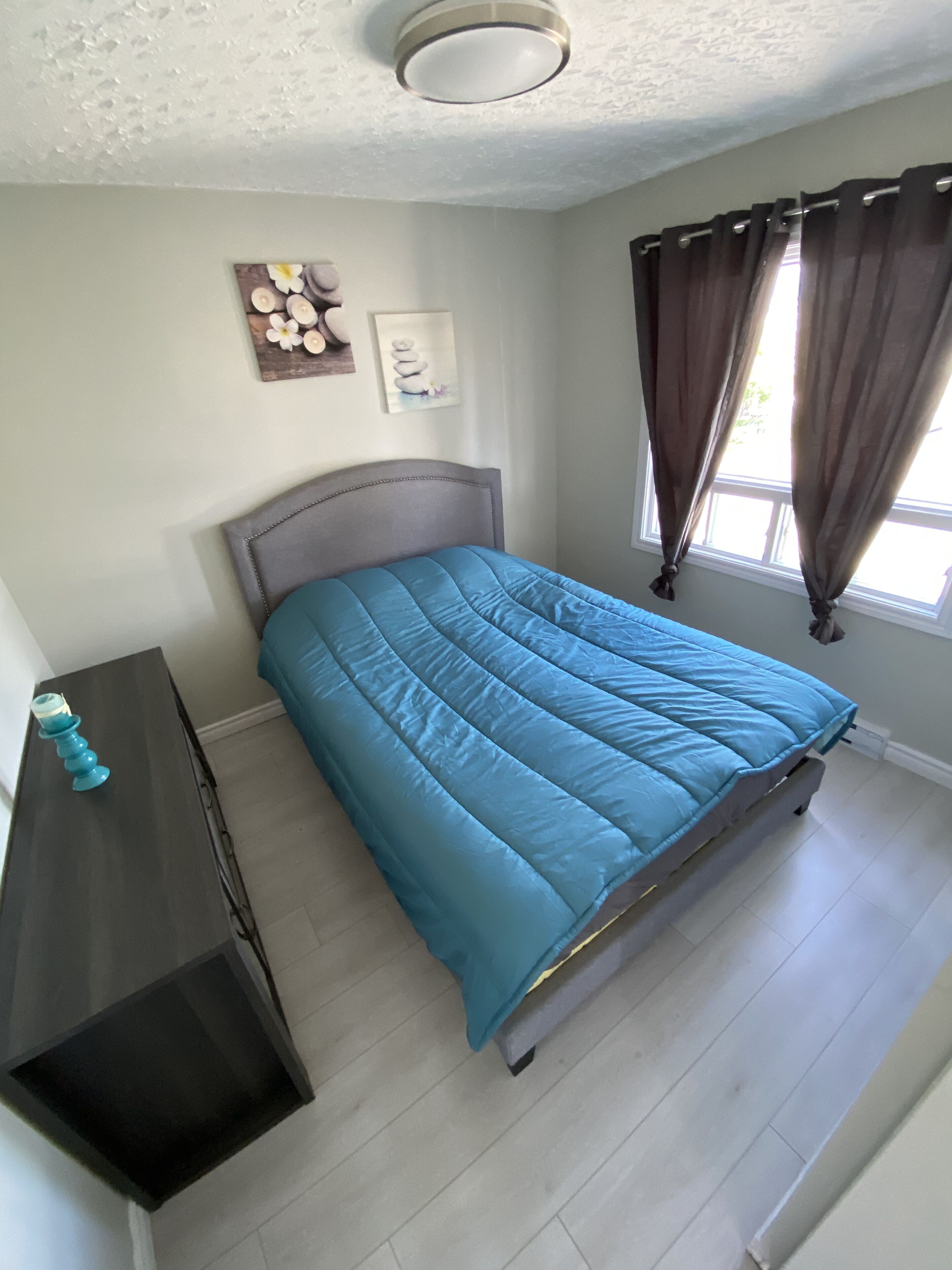 Quarto com cama, mesa de cabeceira, janela com cortinas e obras de arte na parede.