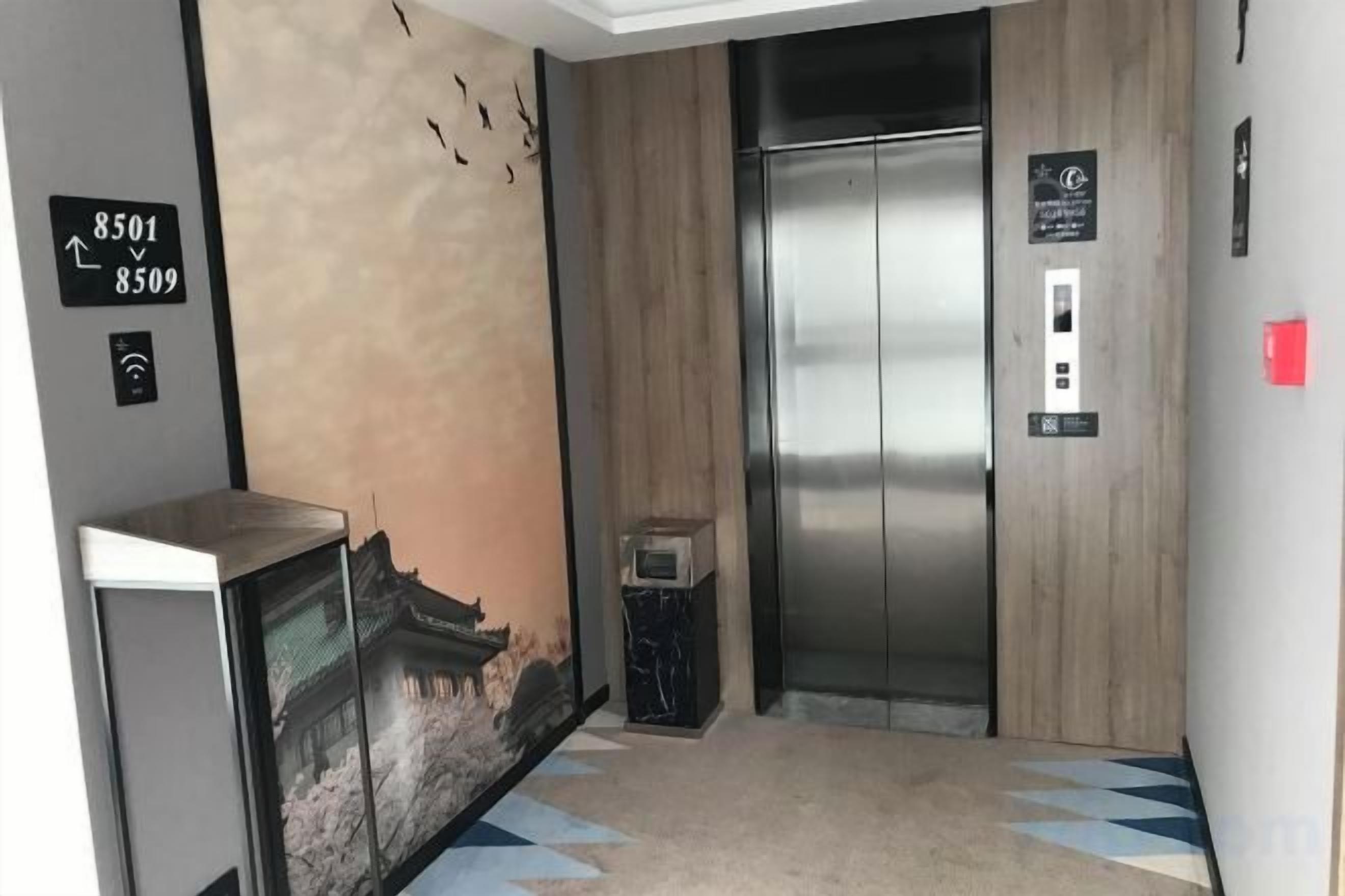 Um elevador com painel de controle, uma placa na parede com números e uma lixeira.