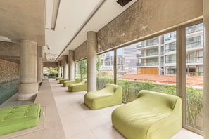 Um corredor com assentos verdes, janelas amplas e vista para edifícios.