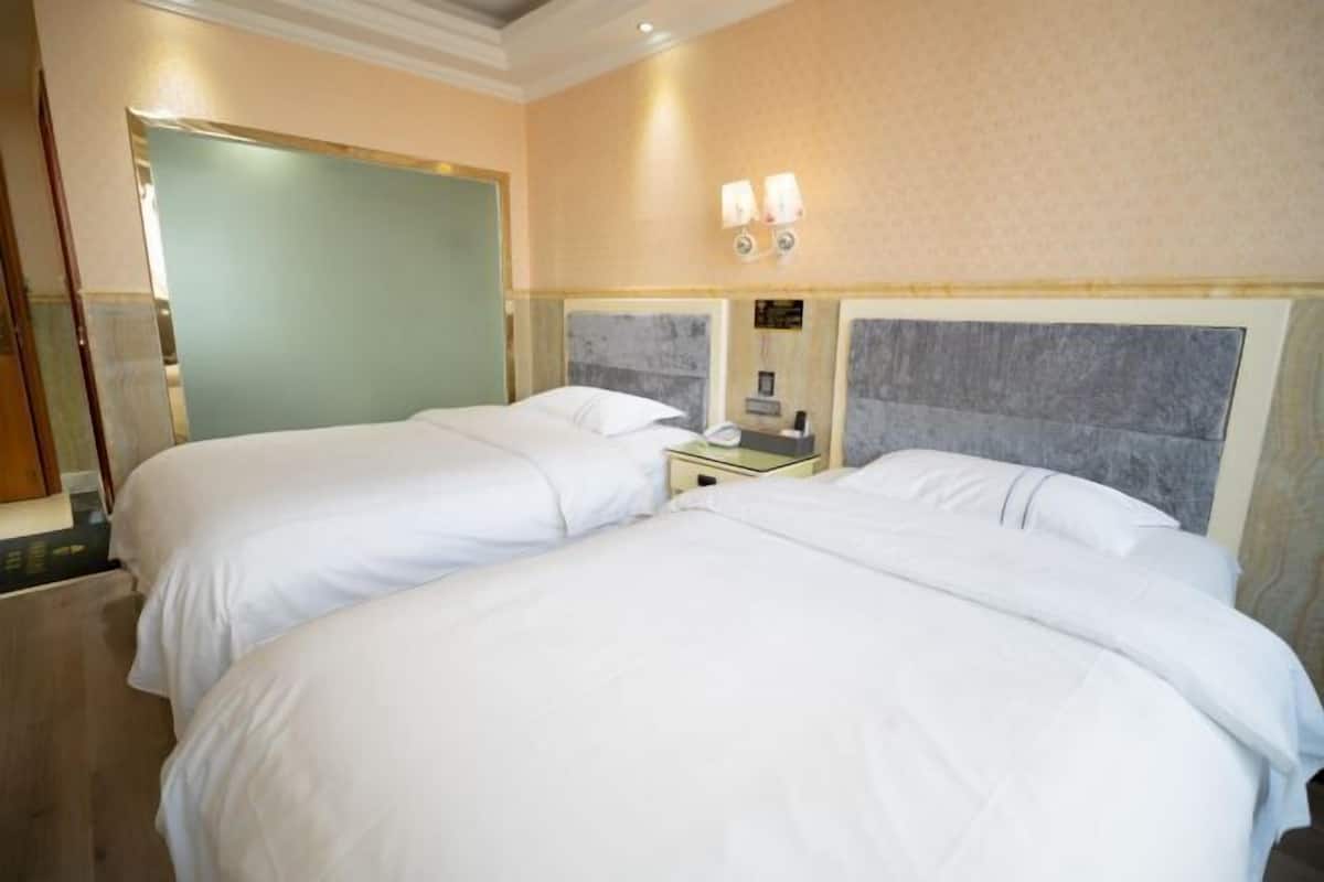Quarto de hotel com duas camas de solteiro, uma mesa de cabeceira com abajur e um espelho fixado na parede.
