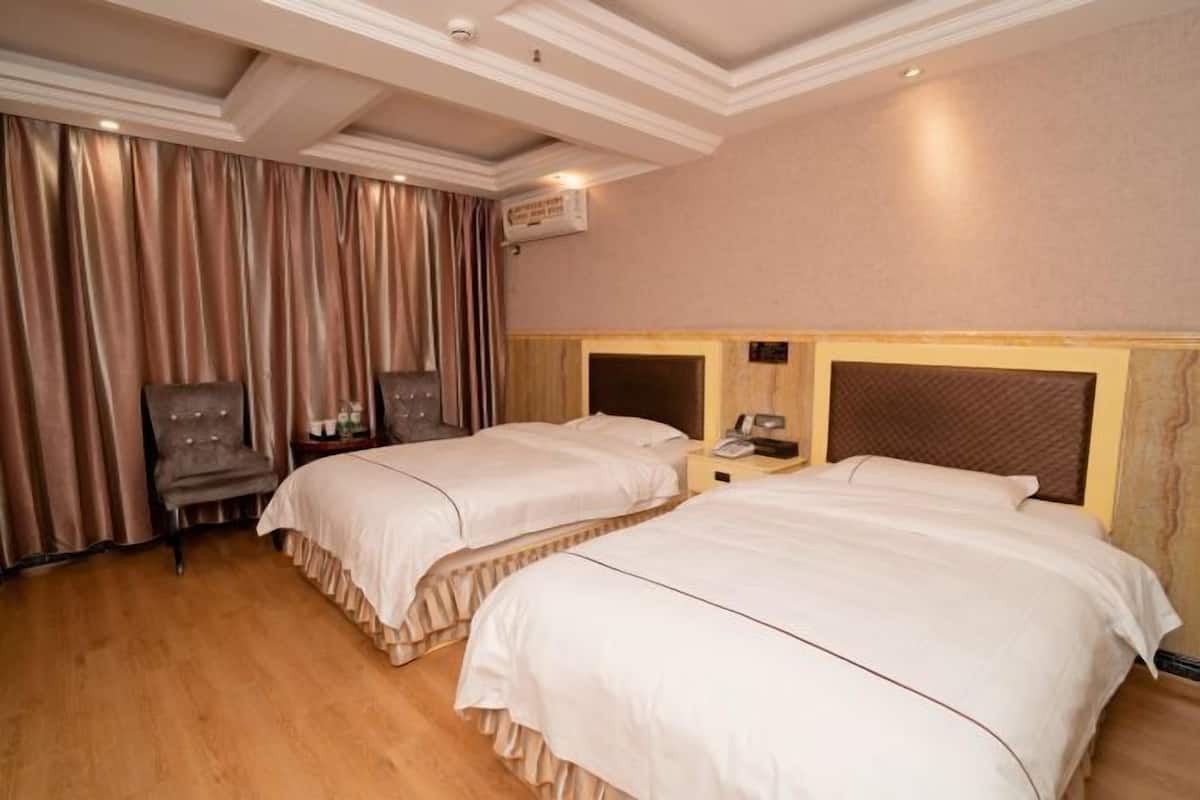 Quarto de hotel com duas camas, uma cadeira, uma mesinha de cabeceira e um aparelho de ar condicionado fixado na parede.