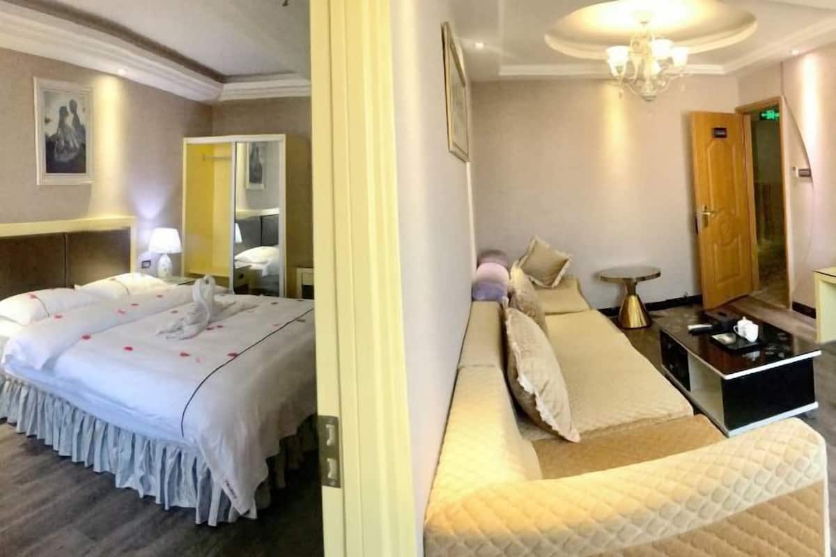 Quarto de hotel com uma cama grande, um sofá, uma mesinha e um espelho.