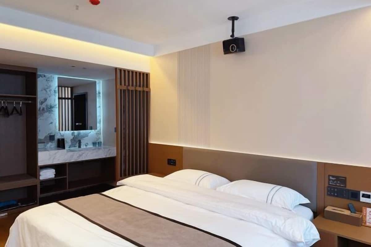 Quarto de hotel moderno com cama grande, guarda-roupa, espelho e painel de controlo na parede.
