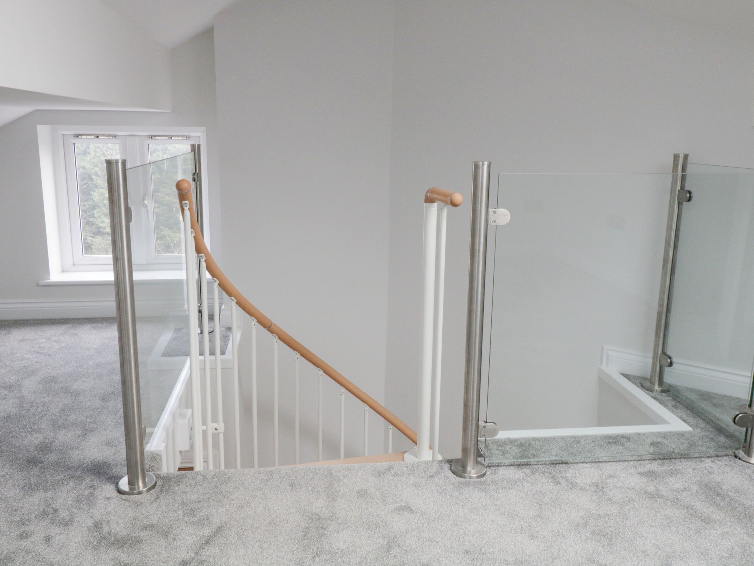 Quarto com carpete cinza, corrimão branco e janela com vista para árvores.
