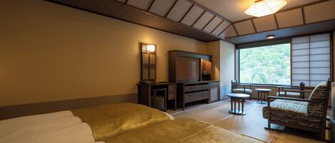 Quarto de hotel em estilo japonês tradicional, com piso de tatame, cama com detalhes dourados, escrivaninha com luminária e vista para o verde através de grandes janelas.
