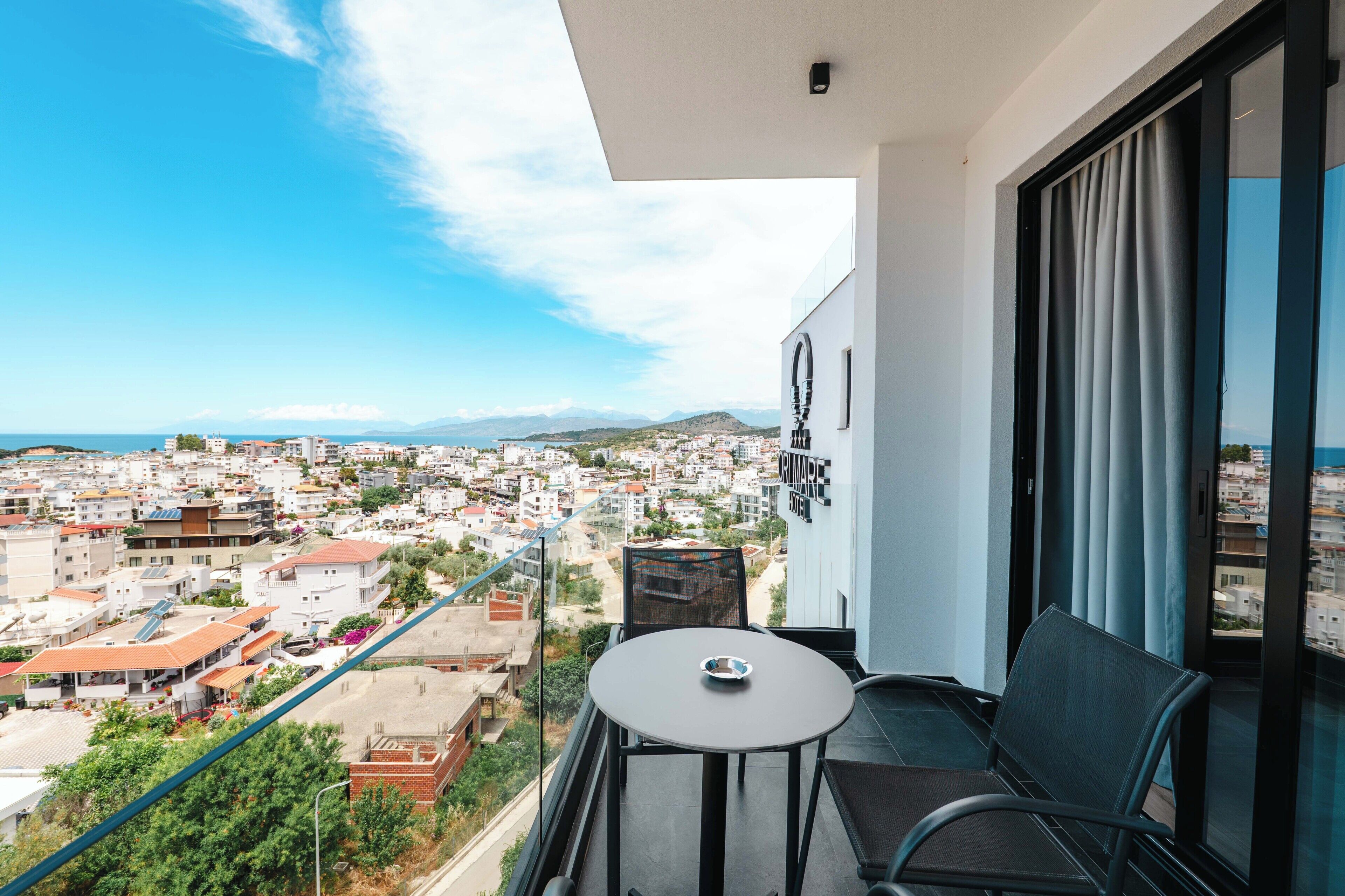 Varanda com mesa e cadeiras, vista para um horizonte urbano com edifícios e montanhas.