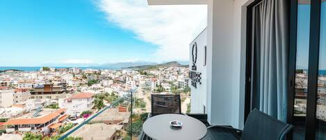 Varanda com mesa e cadeiras, vista para um horizonte urbano com edifícios e montanhas.