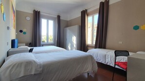 Quarto de hotel com duas camas, uma janela com cortinas, um radiador e uma parede com decorações hexagonais.